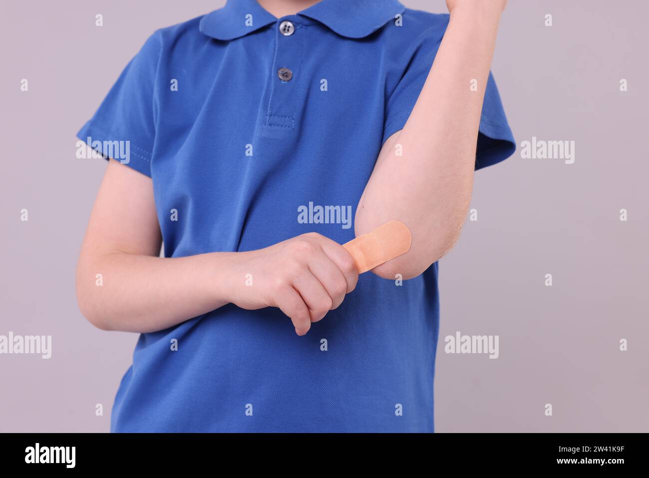 Little boy putting sticking plaster onto elbow against light grey ...