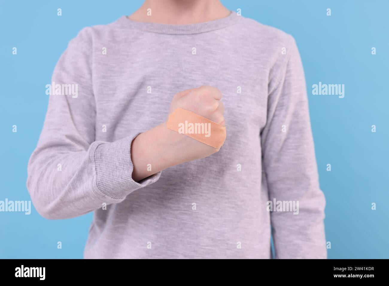 Little boy with sticking plaster on hand against light blue background ...