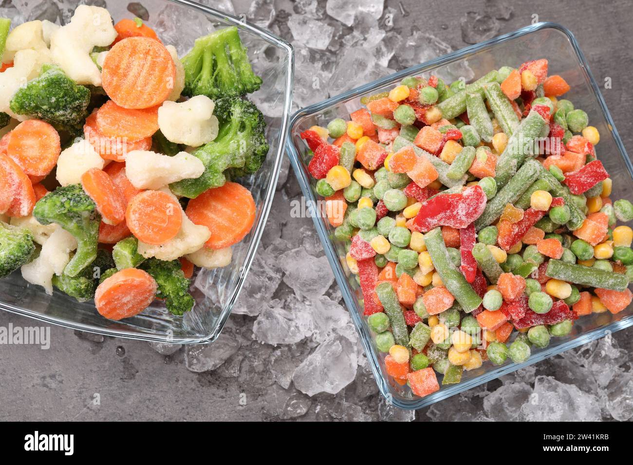 Mix of different frozen vegetables with ice on grey textured table ...