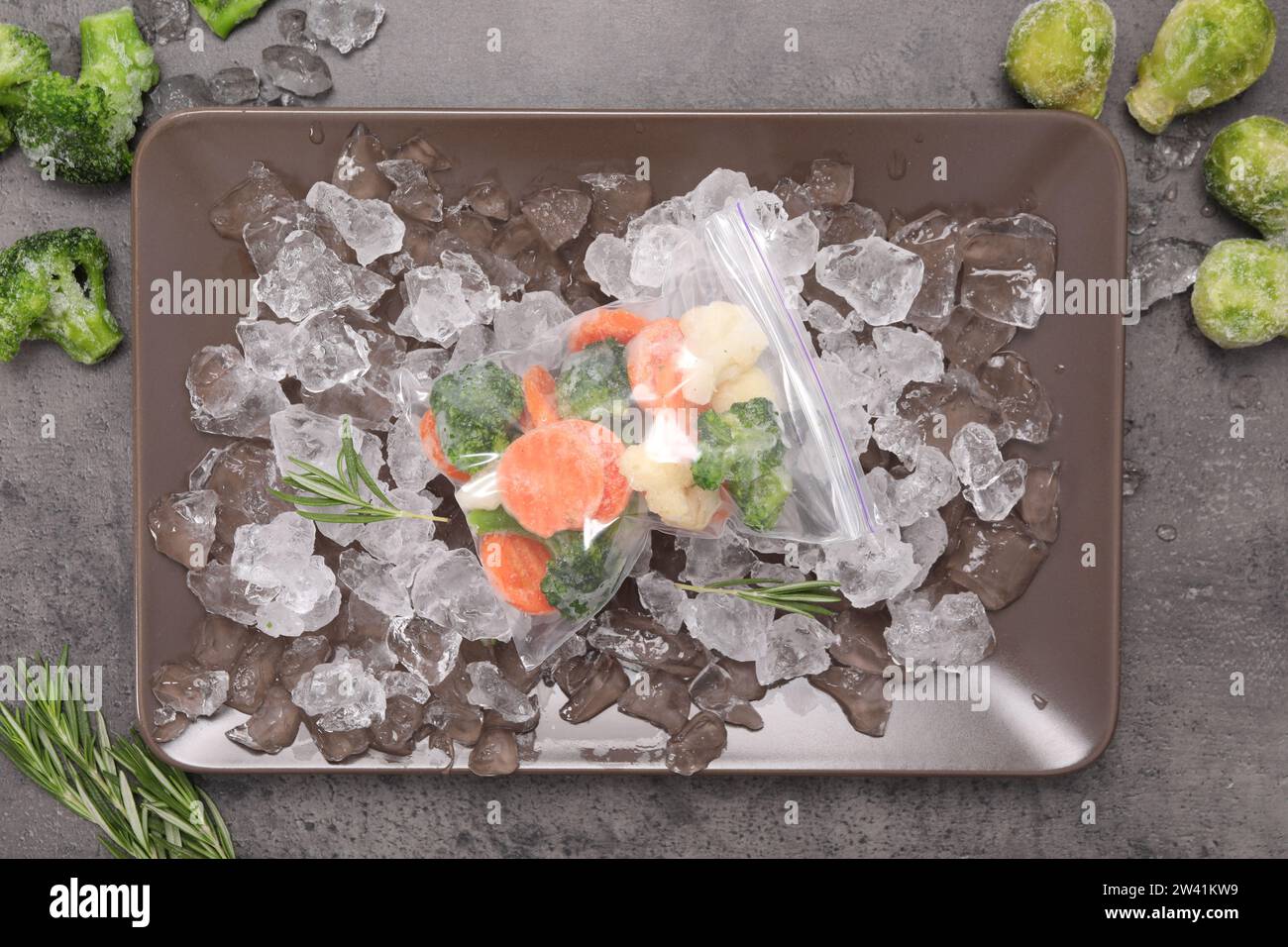Mix of different frozen vegetables with ice on grey table, flat lay ...