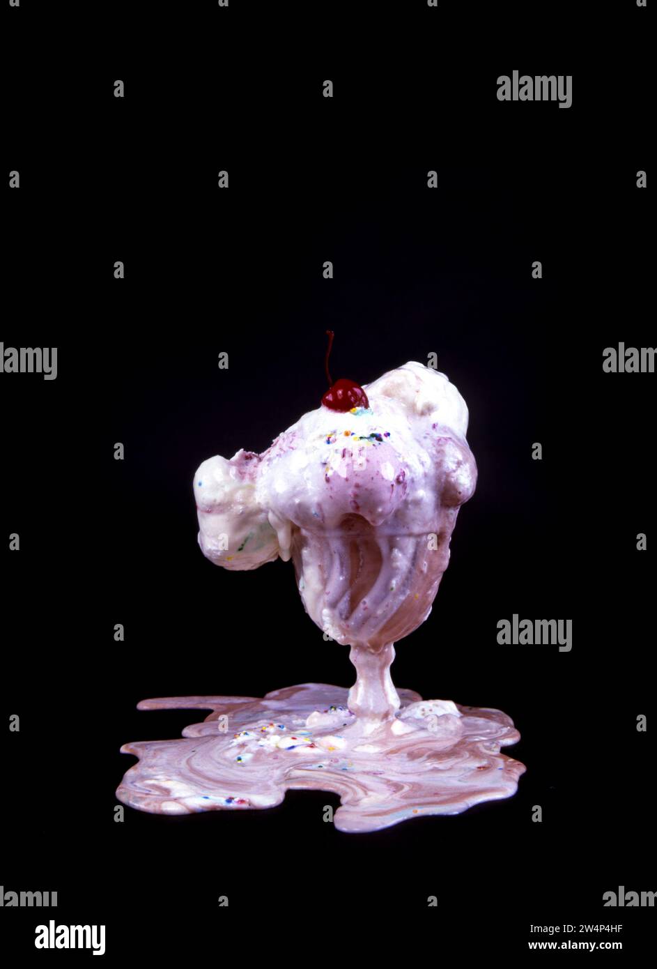 Ice cream sundae with cherry on top melting, with ice cream puddle at ...