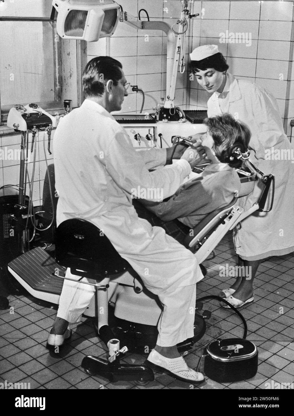 Dentist working on a patient with the help of a dental nurse ca ...