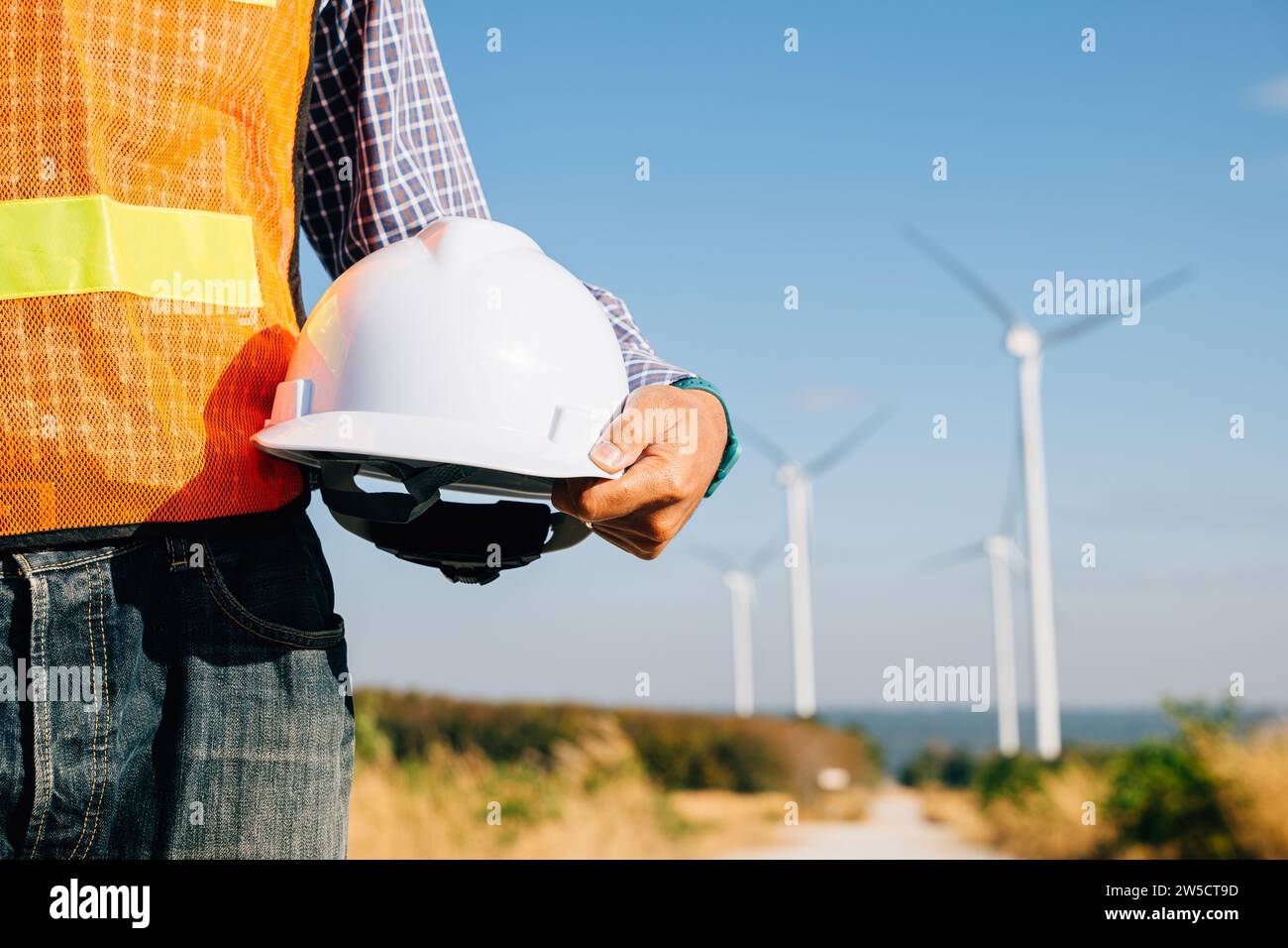 Engineer holding safety helmet stands at windmill field Stock Photo - Alamy