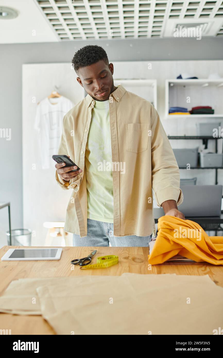 african american designer with smartphone touching fabric samples near ...