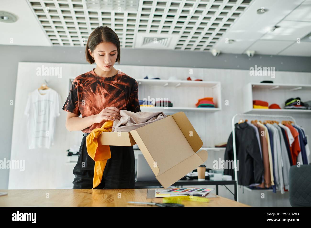 young asian fashion designer unpacking garments from carton box near ...