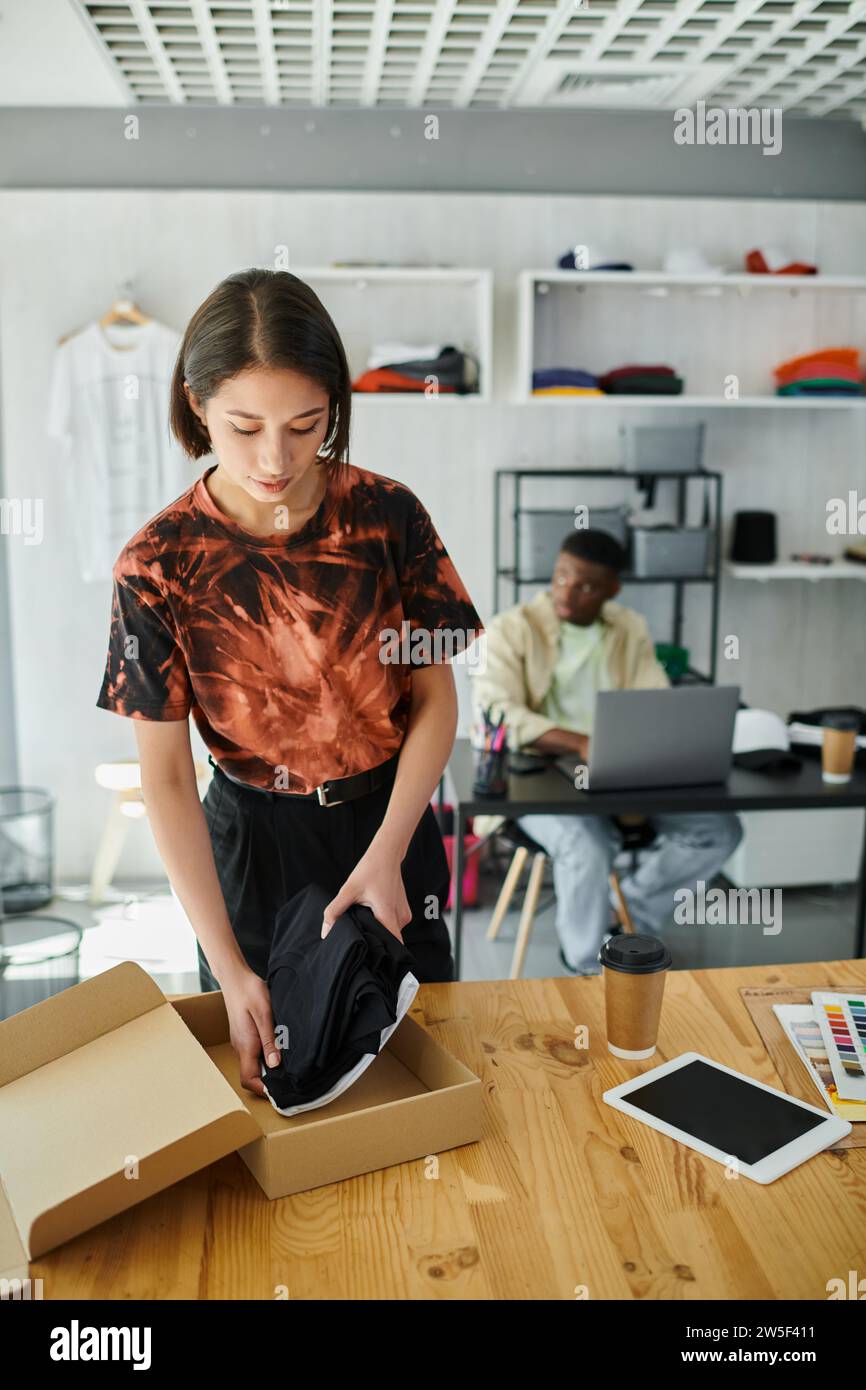 asian woman packing garments in carton box near african american ...