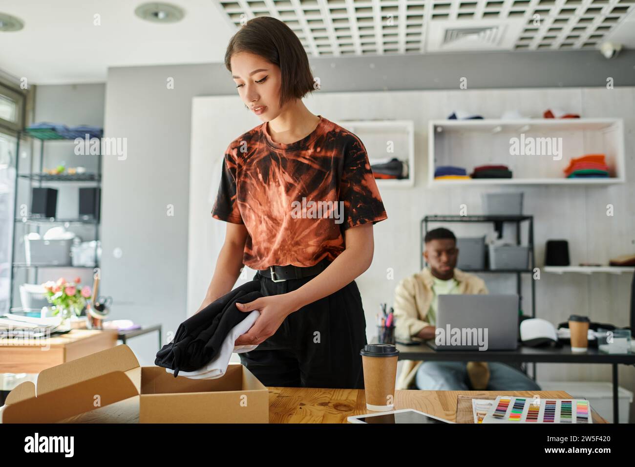 asian woman packing clothes in carton box near african american ...