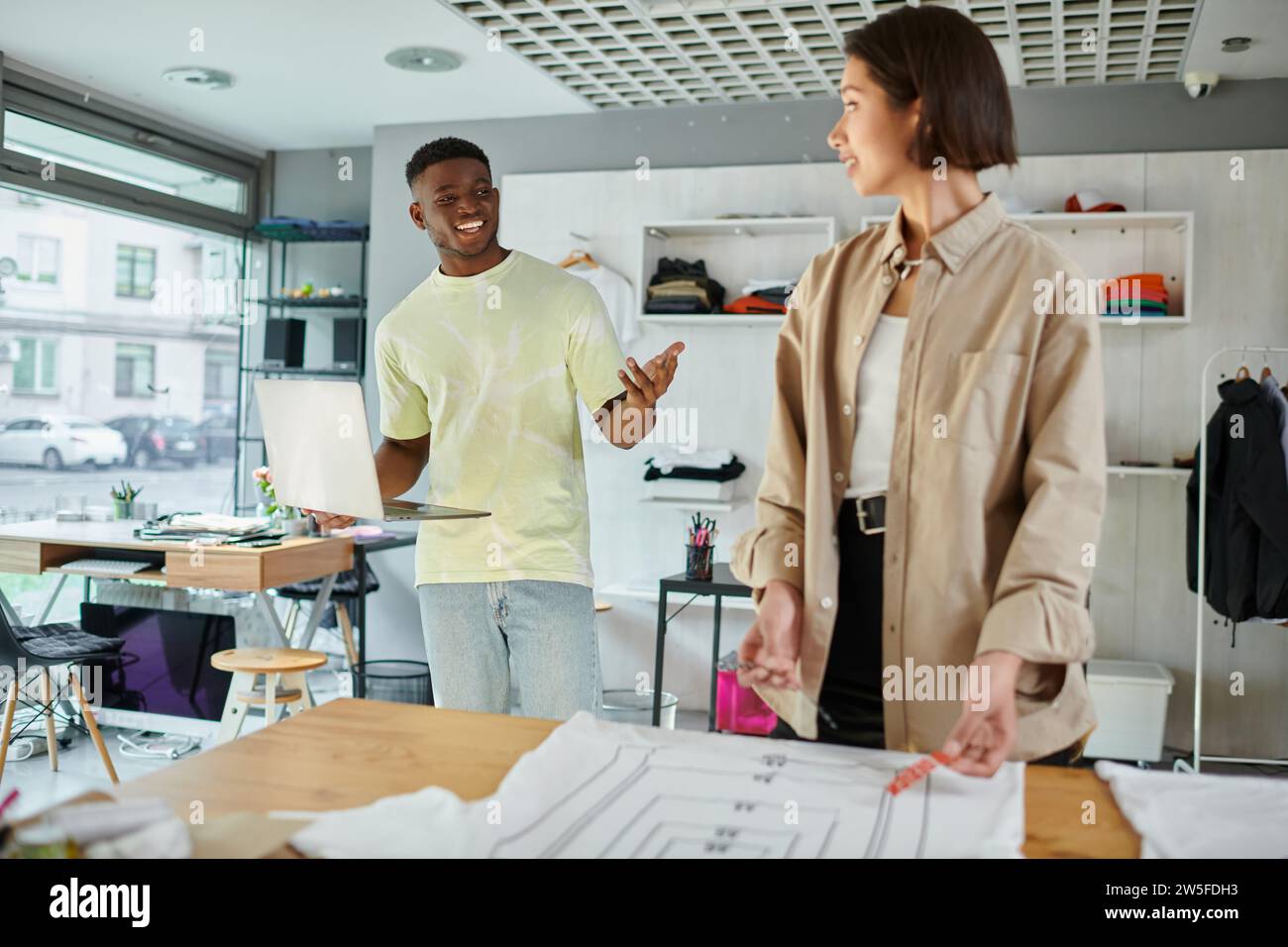 cheerful african american designer with laptop talking to asian ...