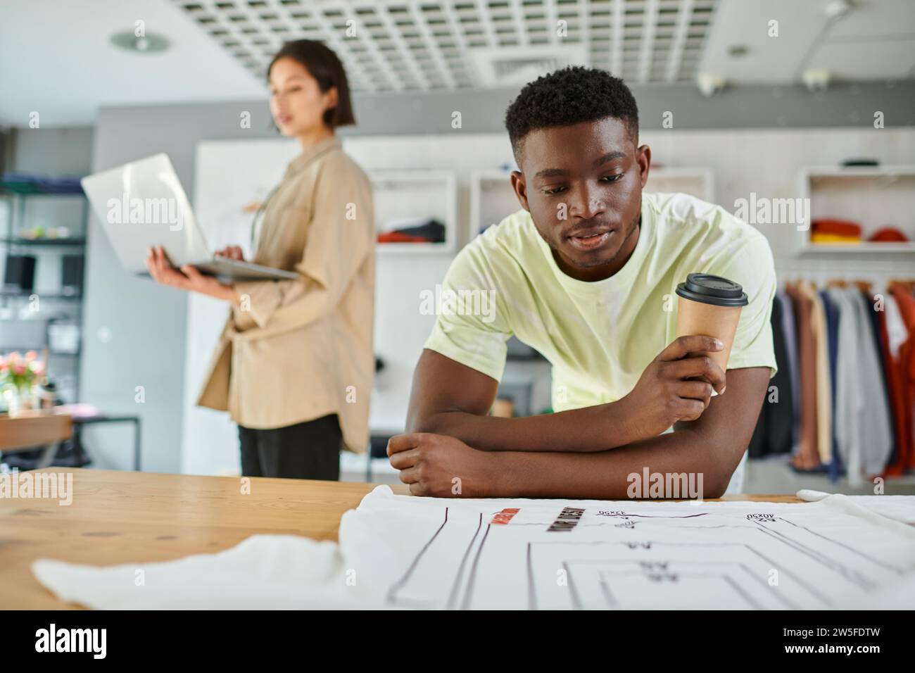 black man with paper cup looking at clothes with format sizes near ...