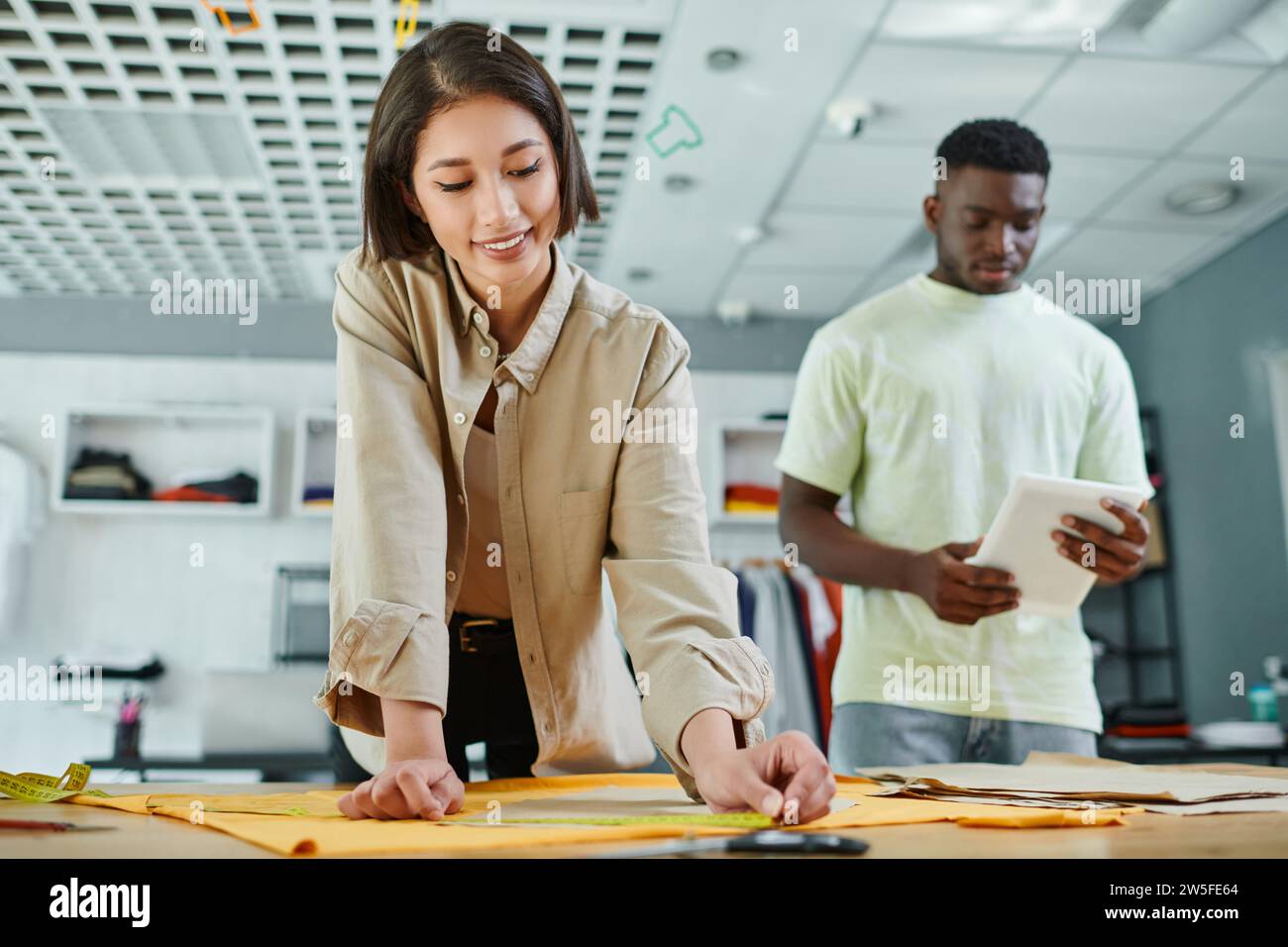 asian designer measuring sewing pattern near african american colleague ...