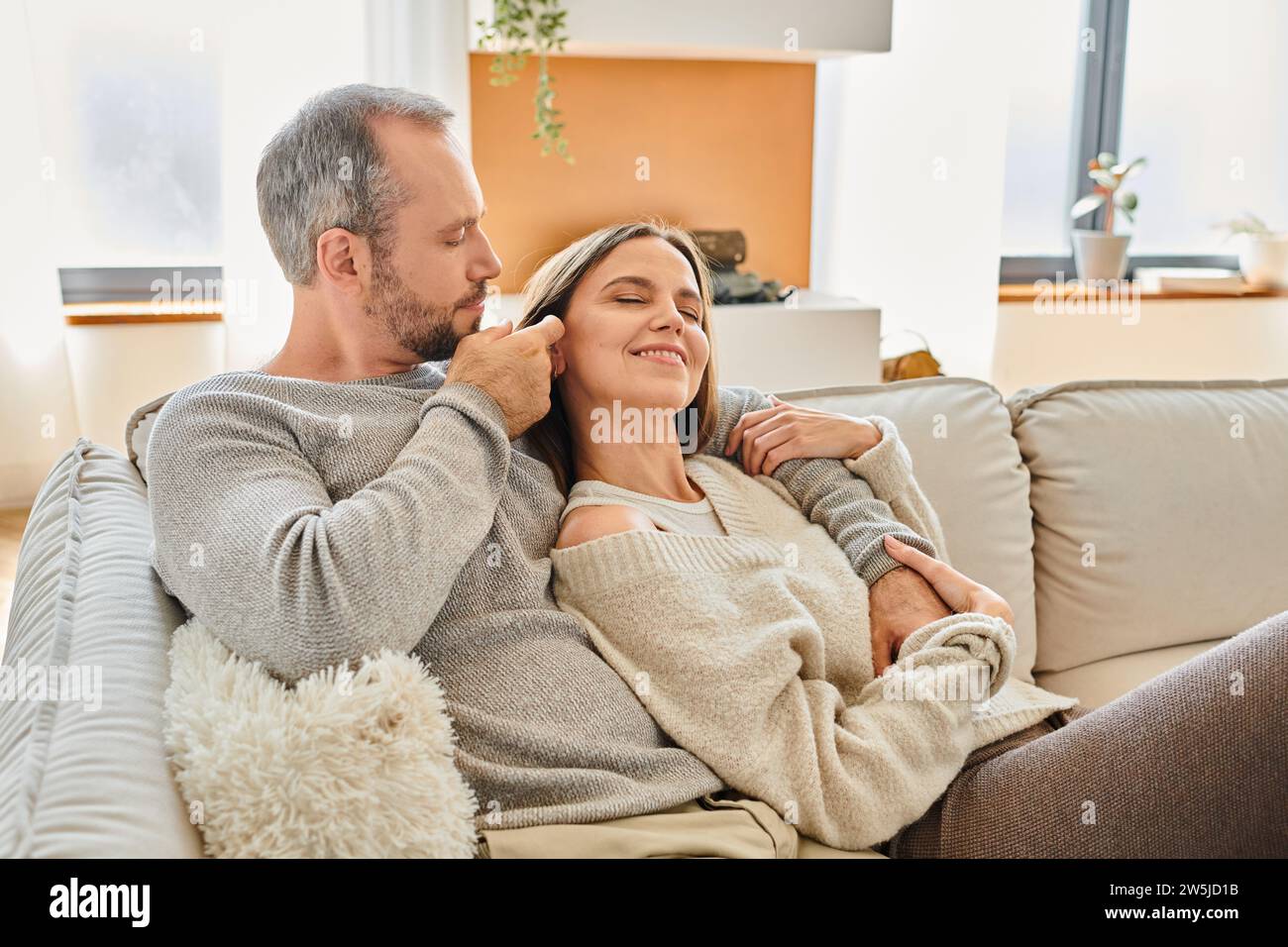 caring man fixing hair of pleased wife while sitting on cozy couch in ...