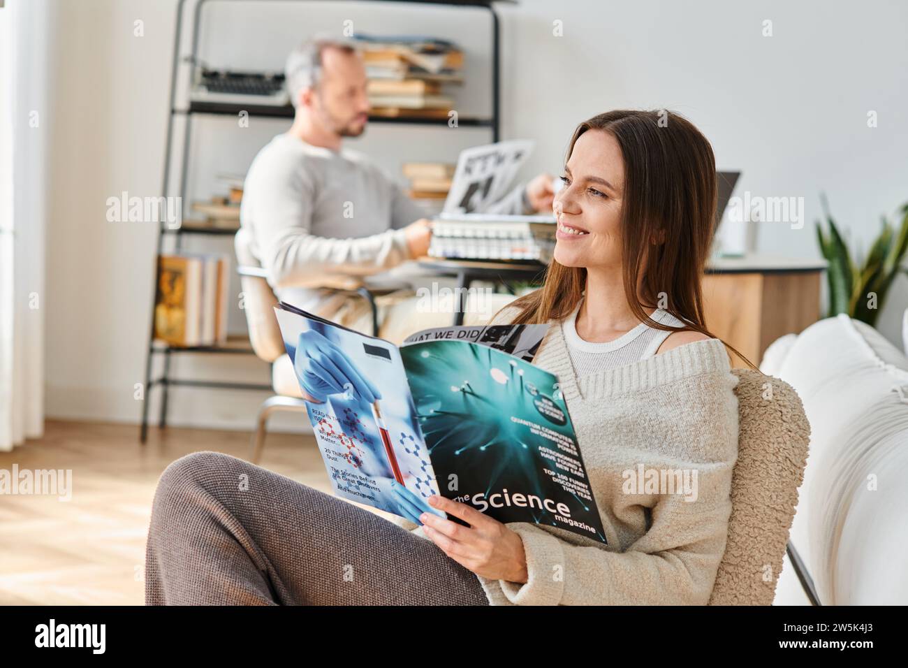 smiling woman reading science magazine near husband in living room ...