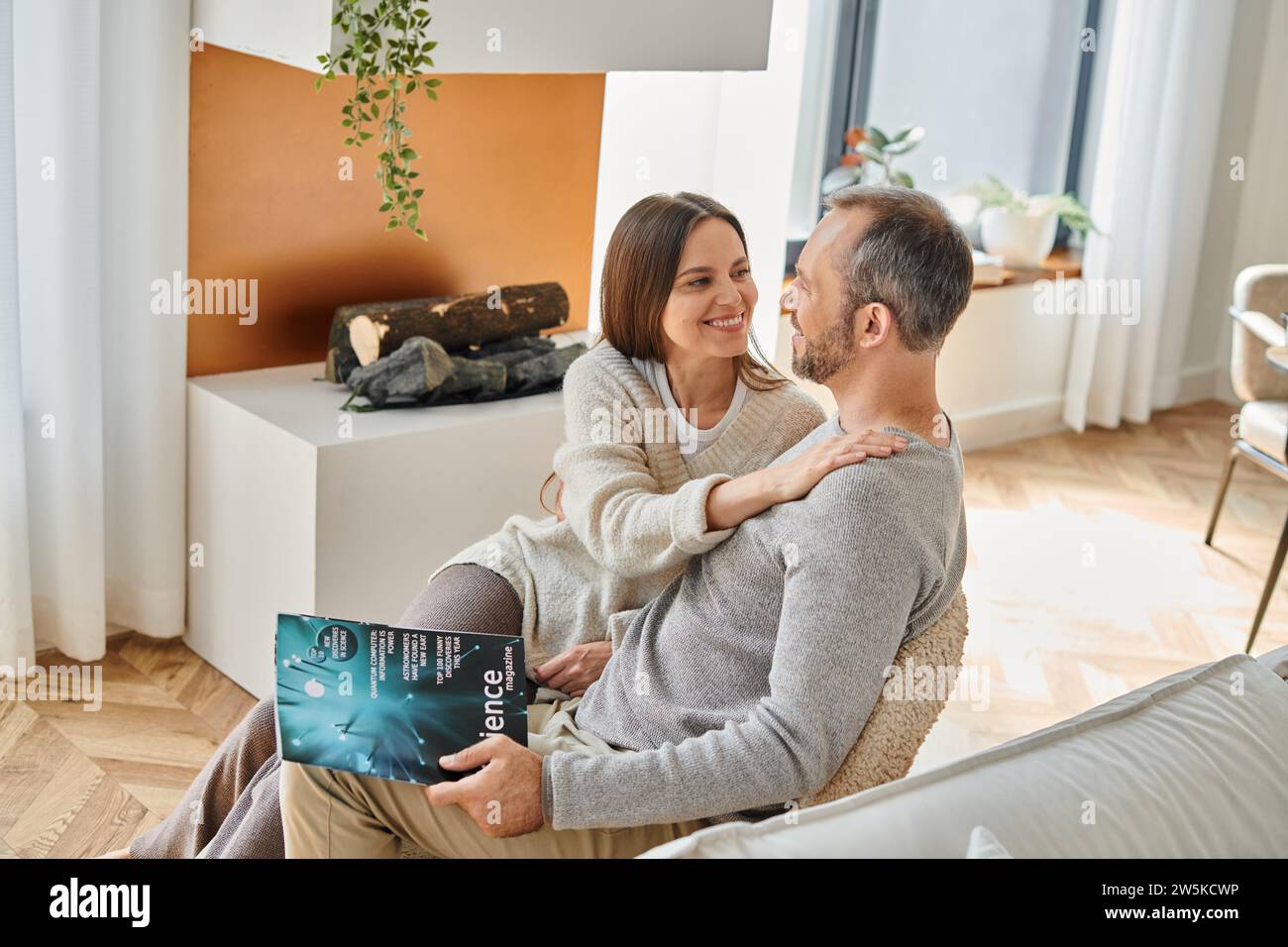 cheerful woman hugging husband sitting with science magazine on couch ...