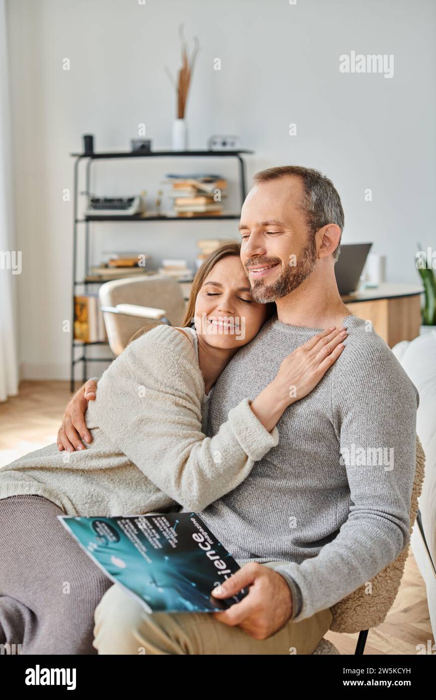 delighted woman hugging husband sitting with science magazine on couch ...