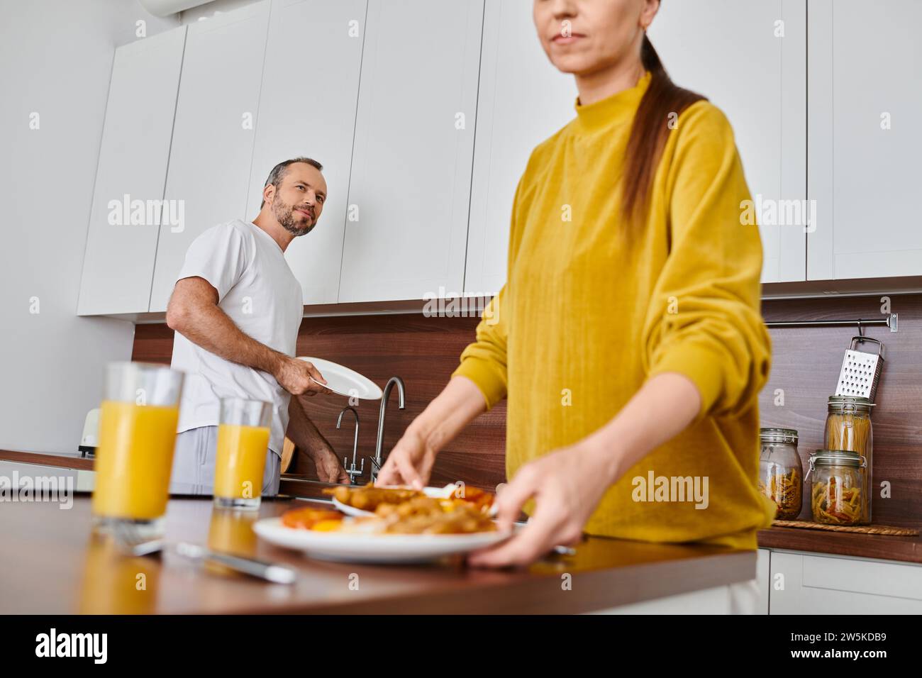 woman serving breakfast near husband washing dishes in kitchen, harmony ...