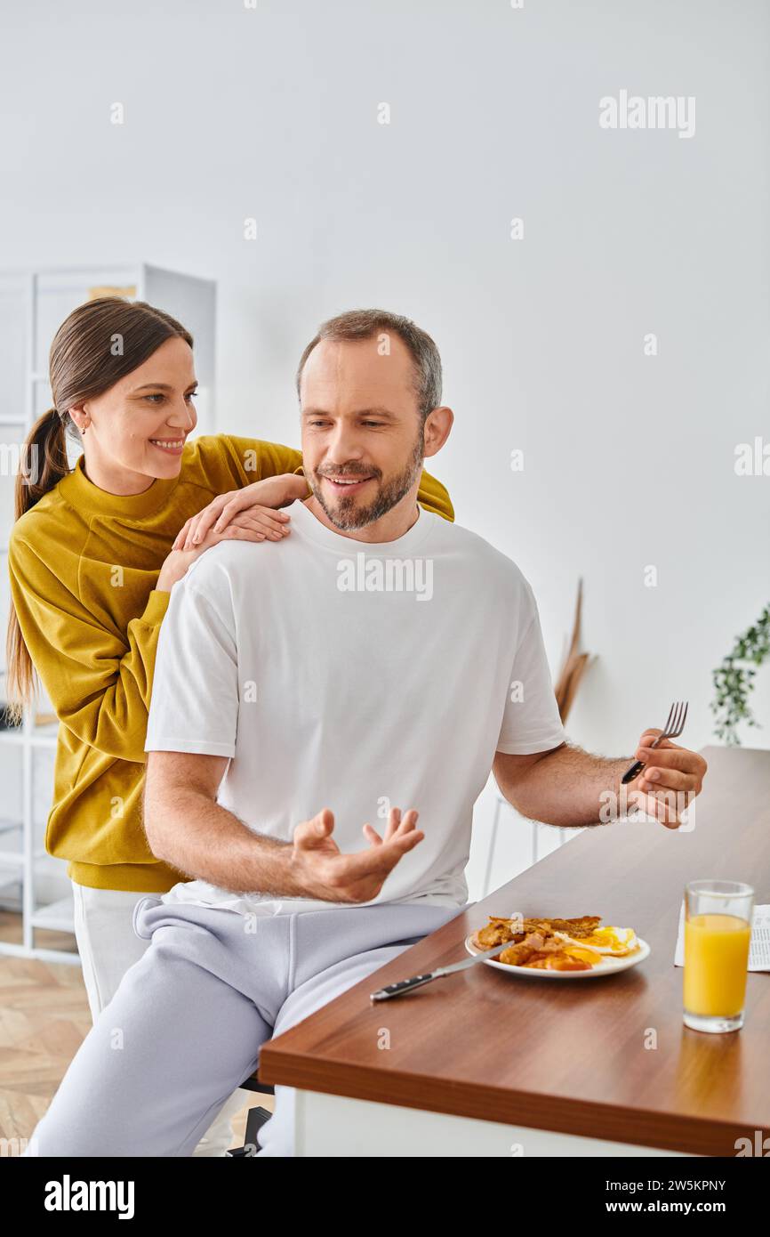 excited man having breakfast and talking to smiling wife in modern ...