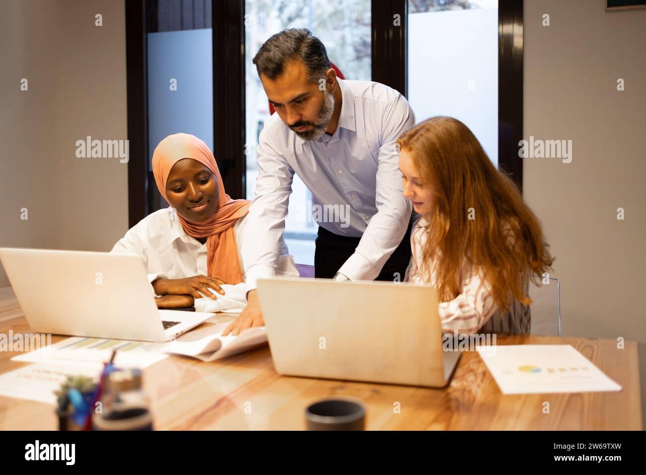 Concentrated diverse colleagues with laptop and documents discussing ...