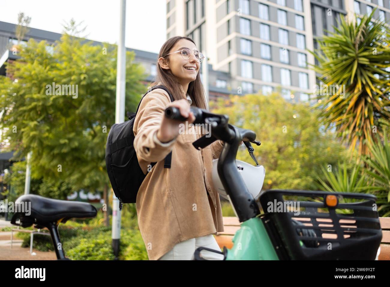 A smiling young female commuter with a backpack prepares to ride a bike ...