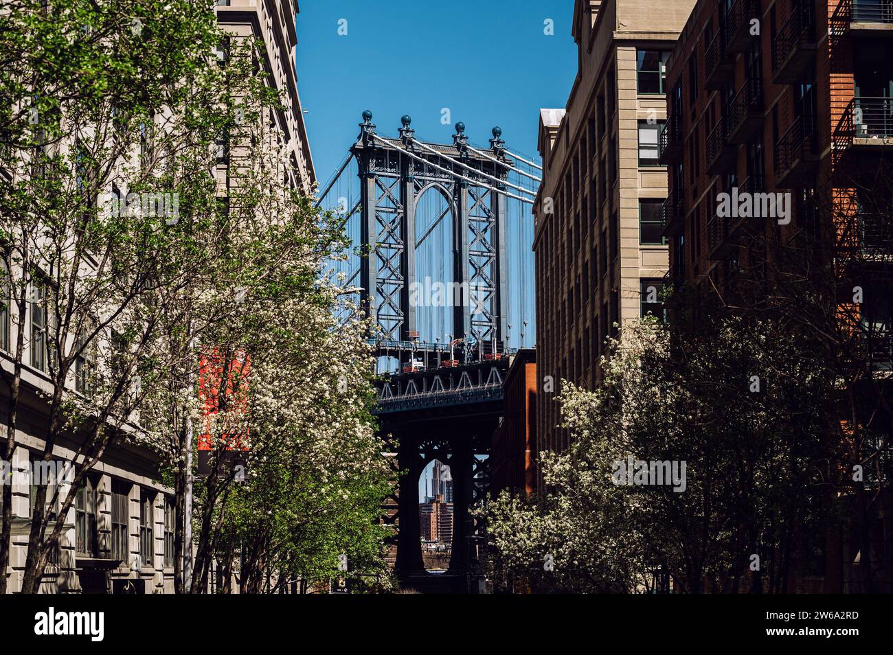 A vibrant street scene in DUMBO, Brooklyn, capturing the iconic Manhattan Bridge framed between ...