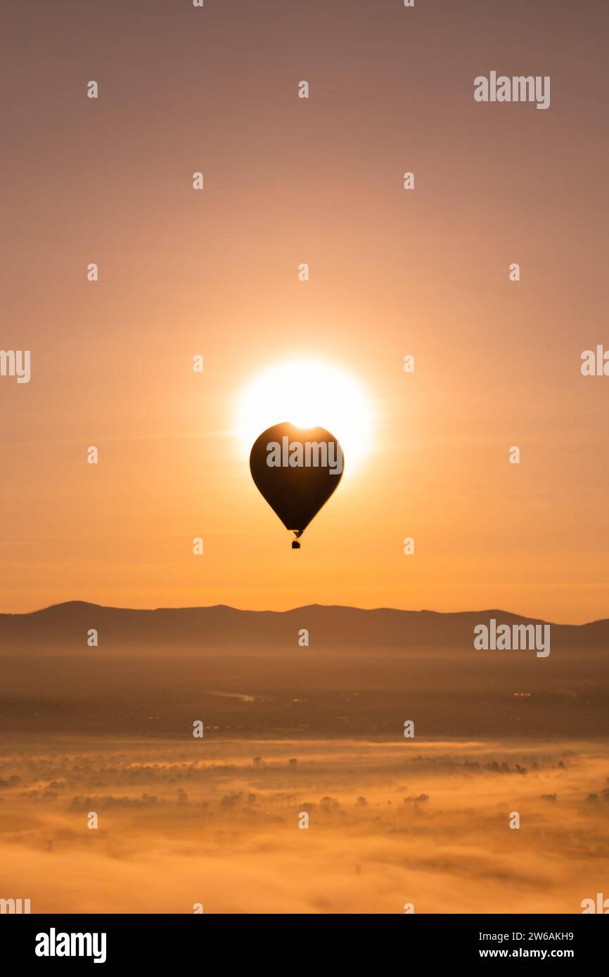 Hot air balloon floats in the golden sunrise sky above a mist-covered ...