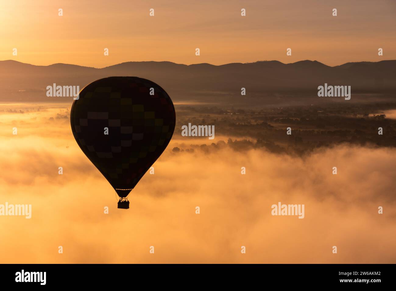 Hot air balloon floats in the golden sunrise sky above a mist-covered ...