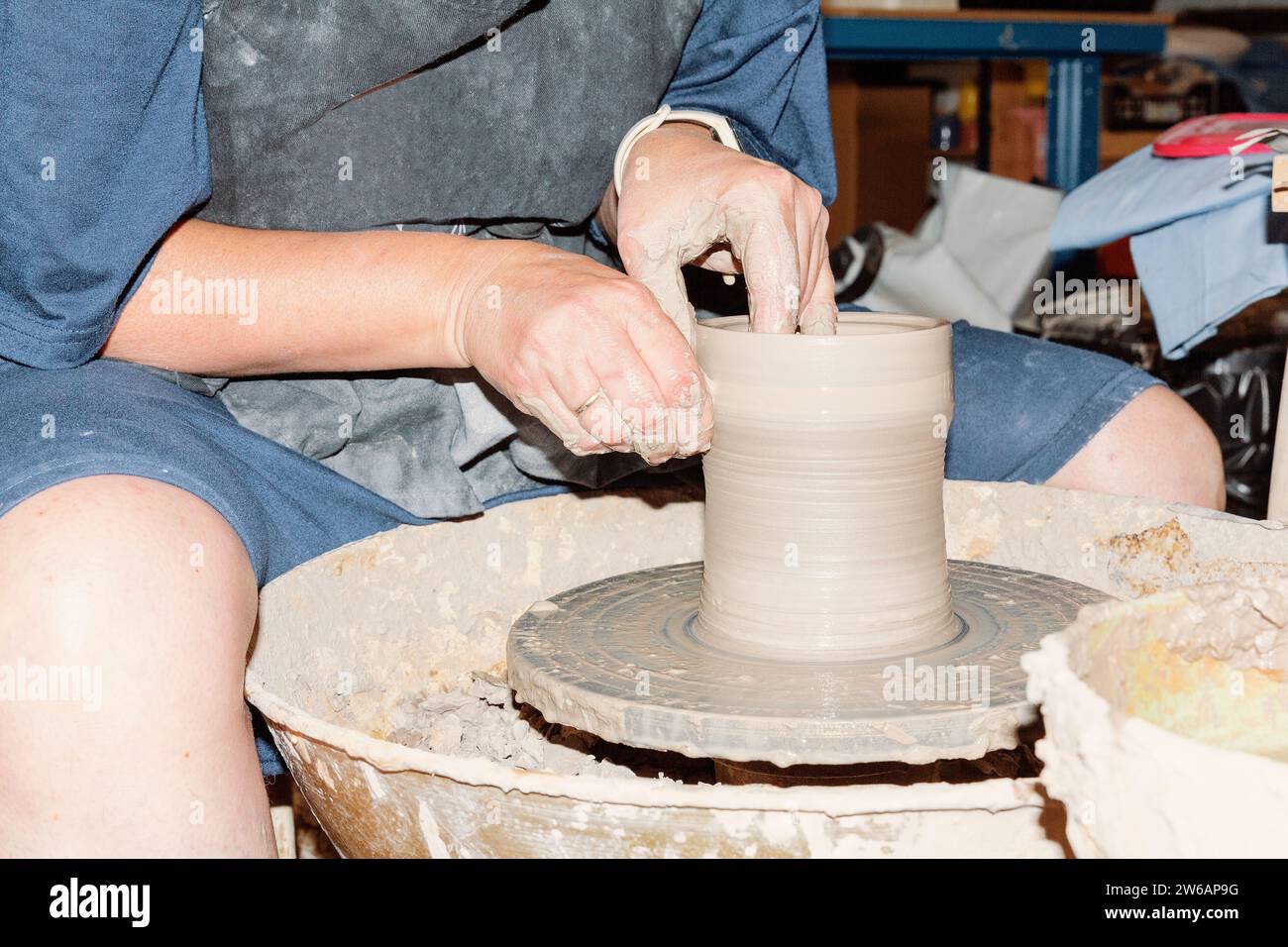 Anonymous craftswoman in apron while sitting at wheel and shaping clay ...