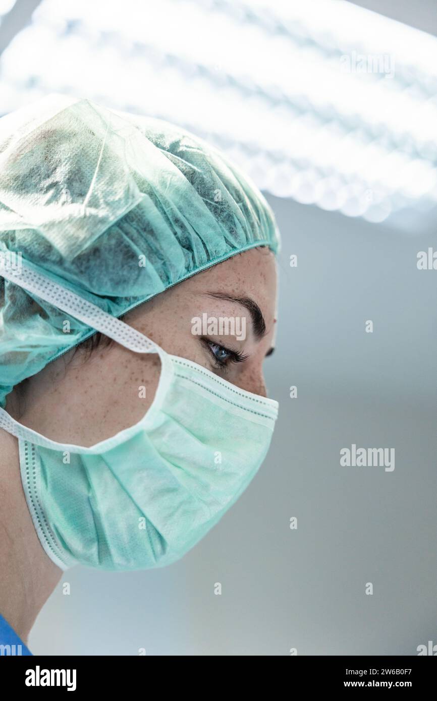 Side view of female surgeon with green cap and protective mask looking ...
