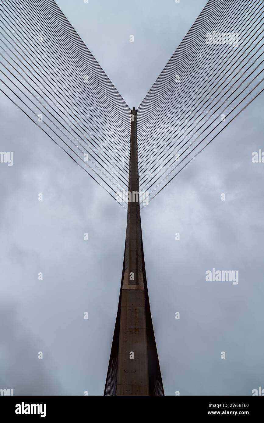 A symmetrical upward view of a tall suspension bridge against a moody ...