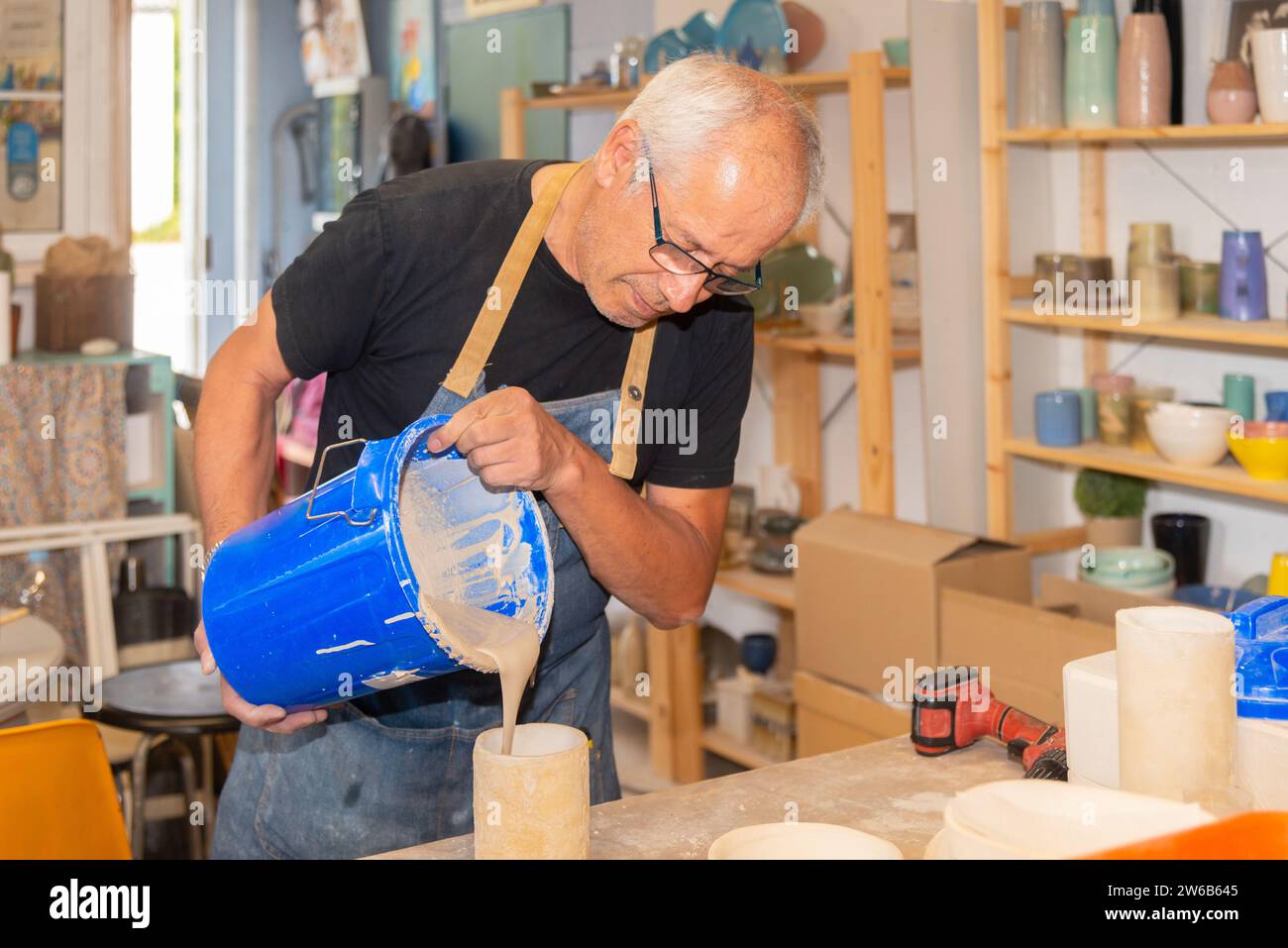 Side view of mature male artisan in apron and eyeglasses looking down ...
