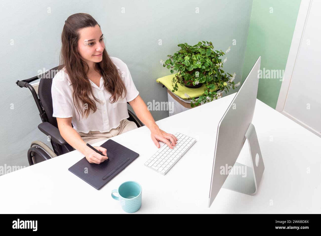 A cheerful woman in a wheelchair works at her desk with a graphics ...