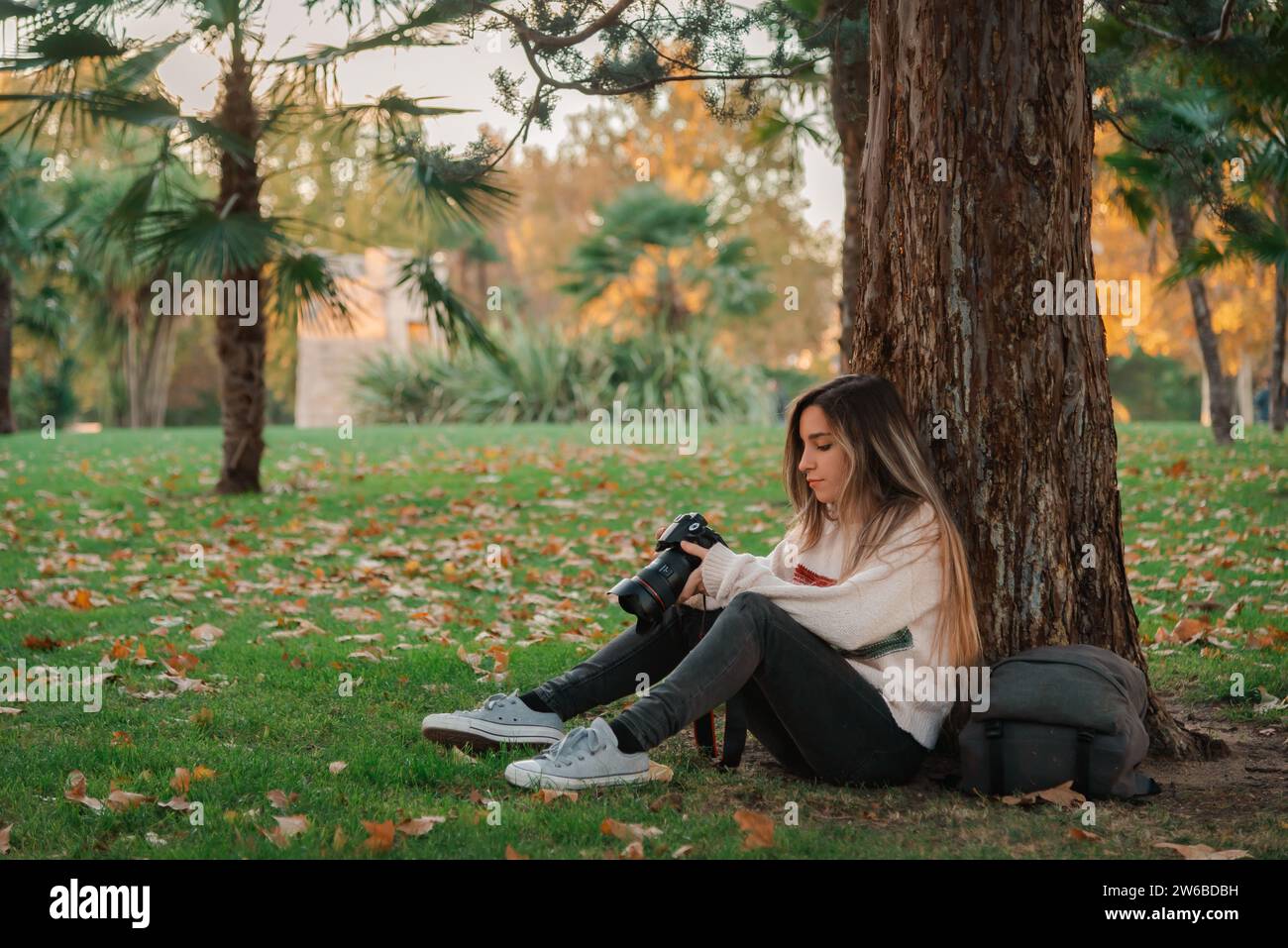 A young female photographer sits under a tree examining her camera in ...