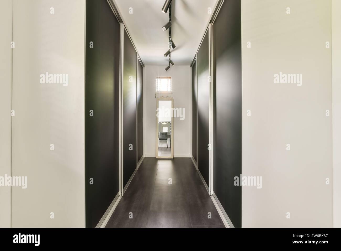 A sleek, empty hallway featuring dark wood floors, track lights, and ...