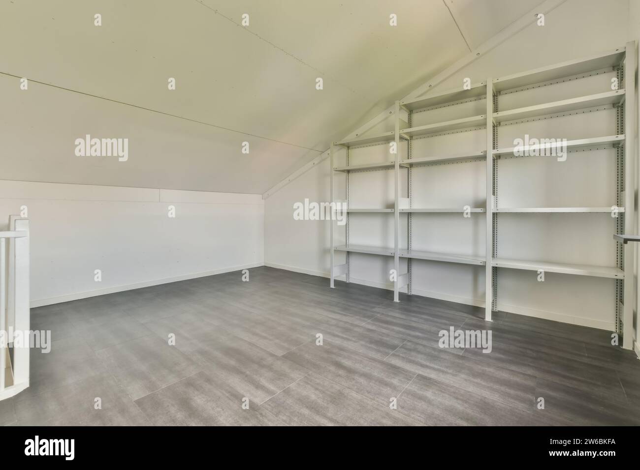 An empty attic space with white walls and gray flooring, featuring ...