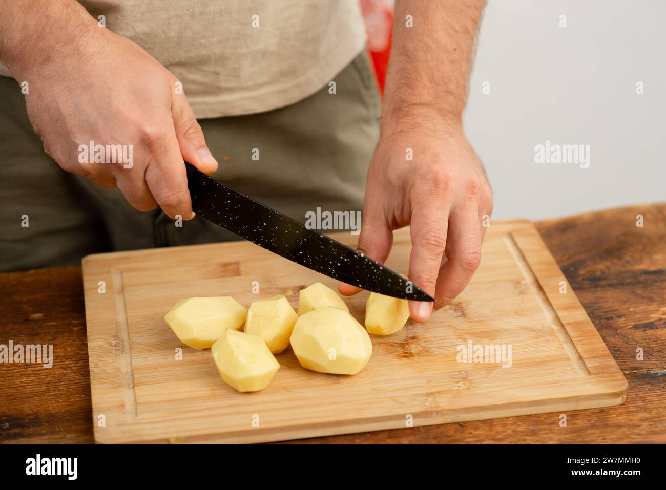 A person cutting peeled potatoes on a bamboo cutting board, meal ...