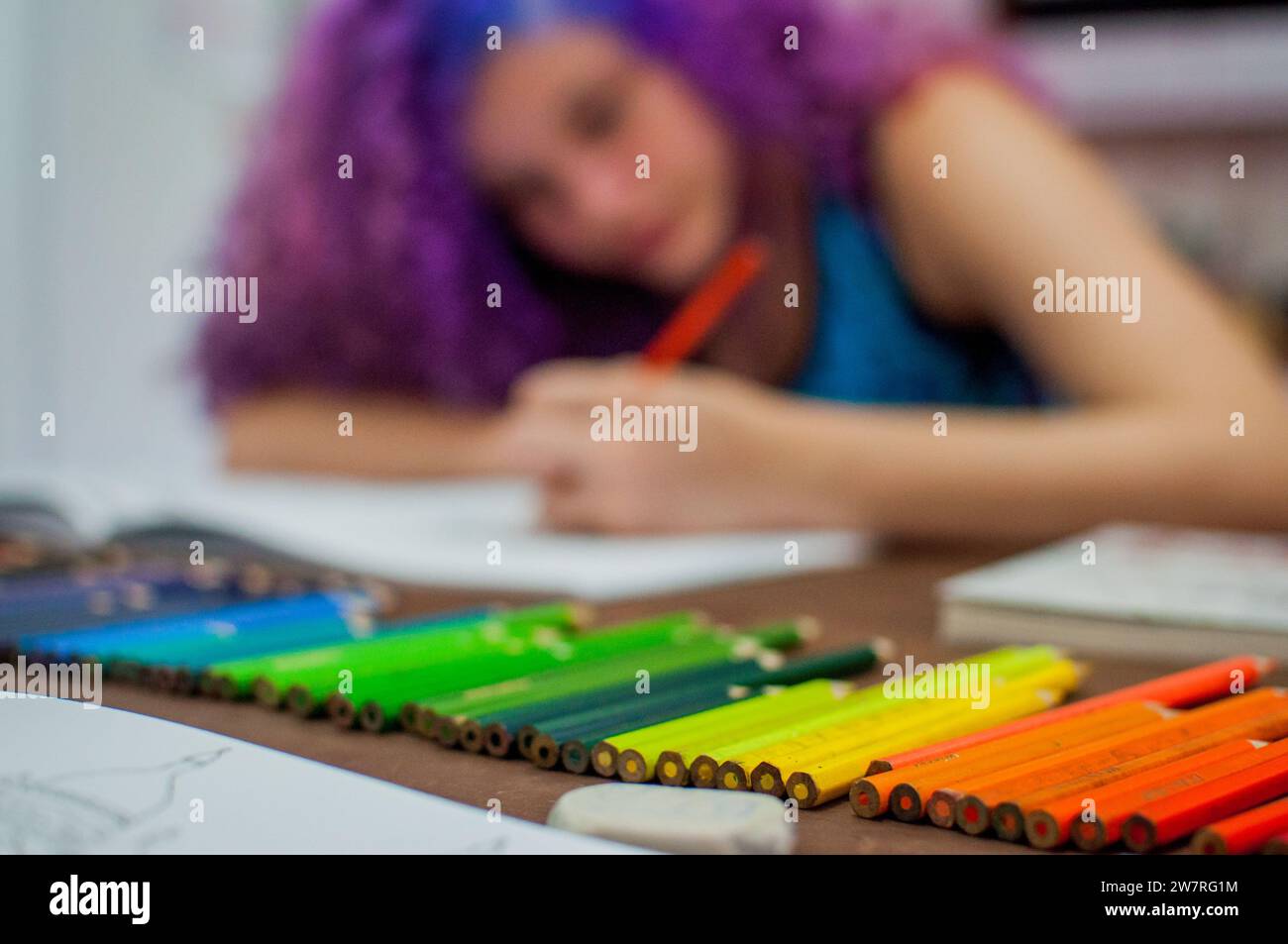 Portrait of girl with lilac hair drawing, writing. Blurred person ...