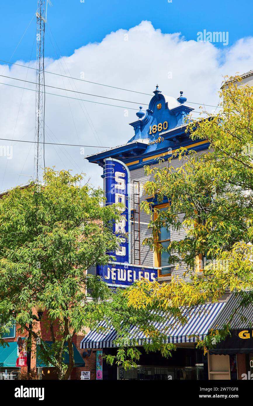 Retro sign on shop behind lush green trees in summer with blue sky and ...