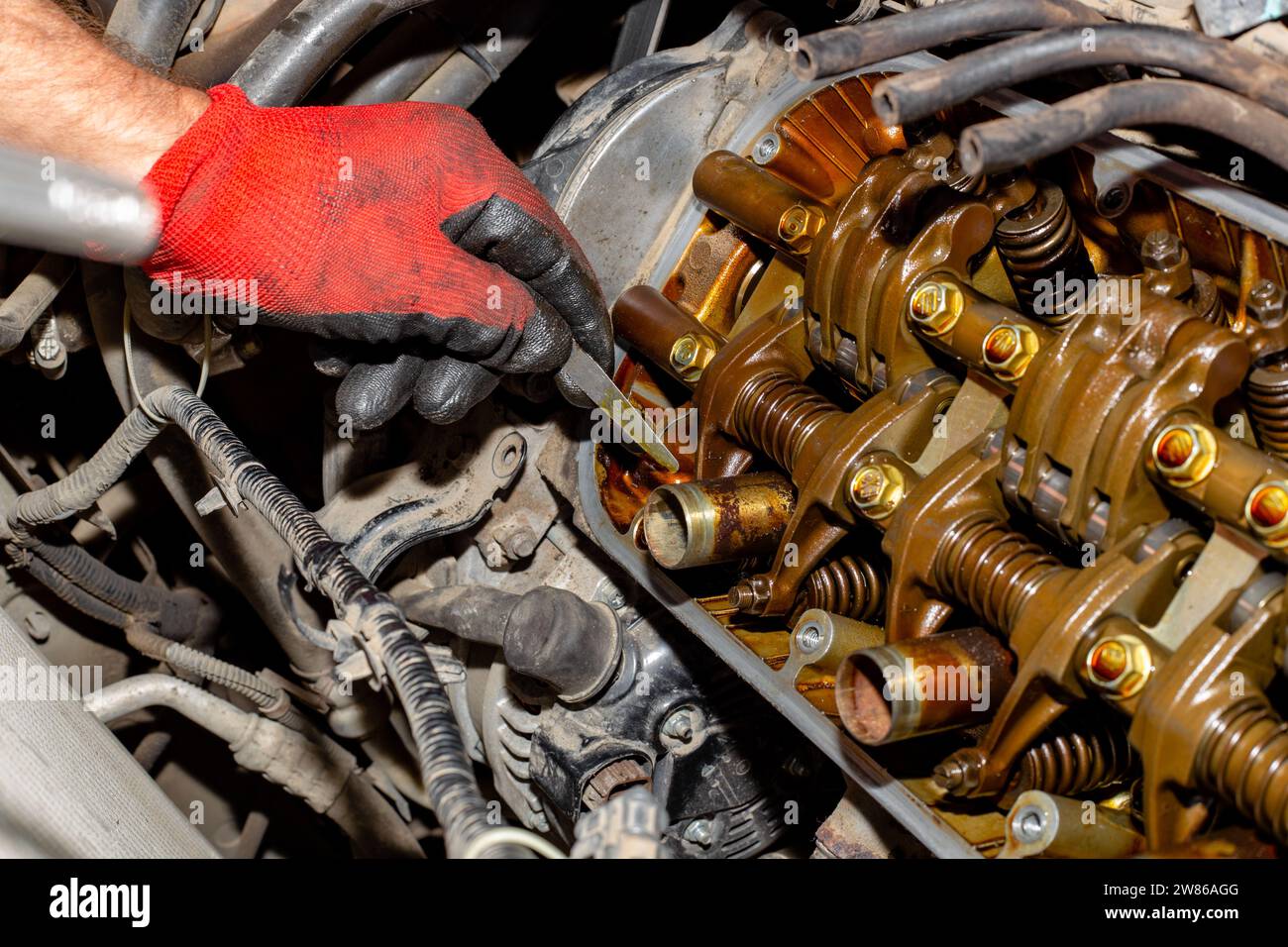 Car repairs. An auto mechanic adjusts the thermal clearances of the ...