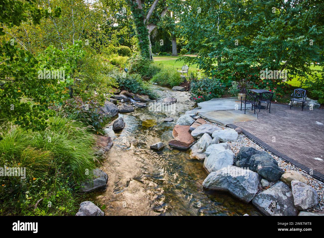 Serene Garden with Stream and Patio Furniture, Lush Greenery View Stock ...