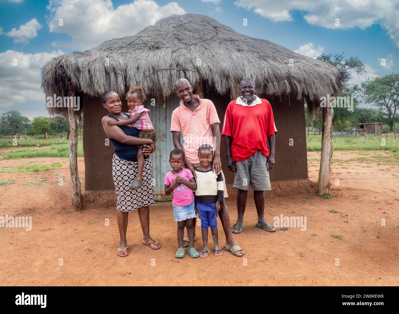 african family village, father, mother and grandfather together with the kids in front of a hut ...