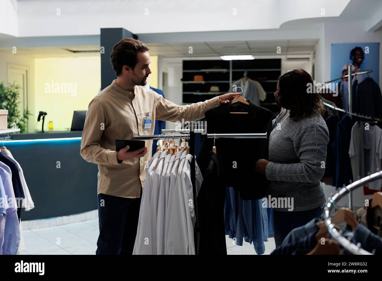 Clothing store employee showing jacket on hanger to customer, offering ...