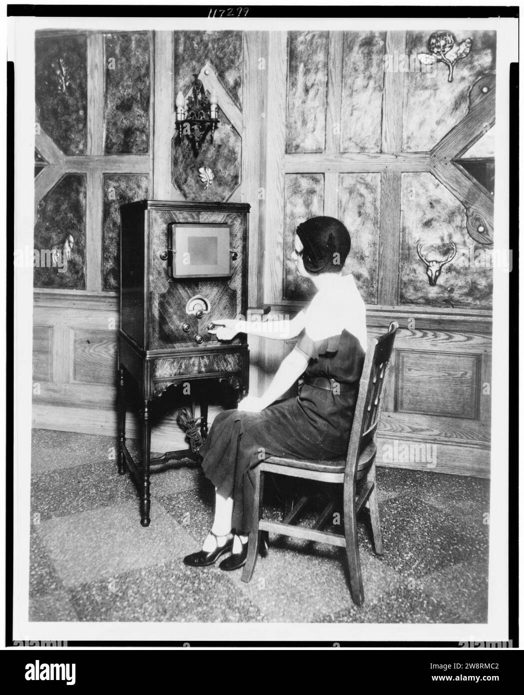 Woman, full-length, seated, facing left, turning dial of a console ...