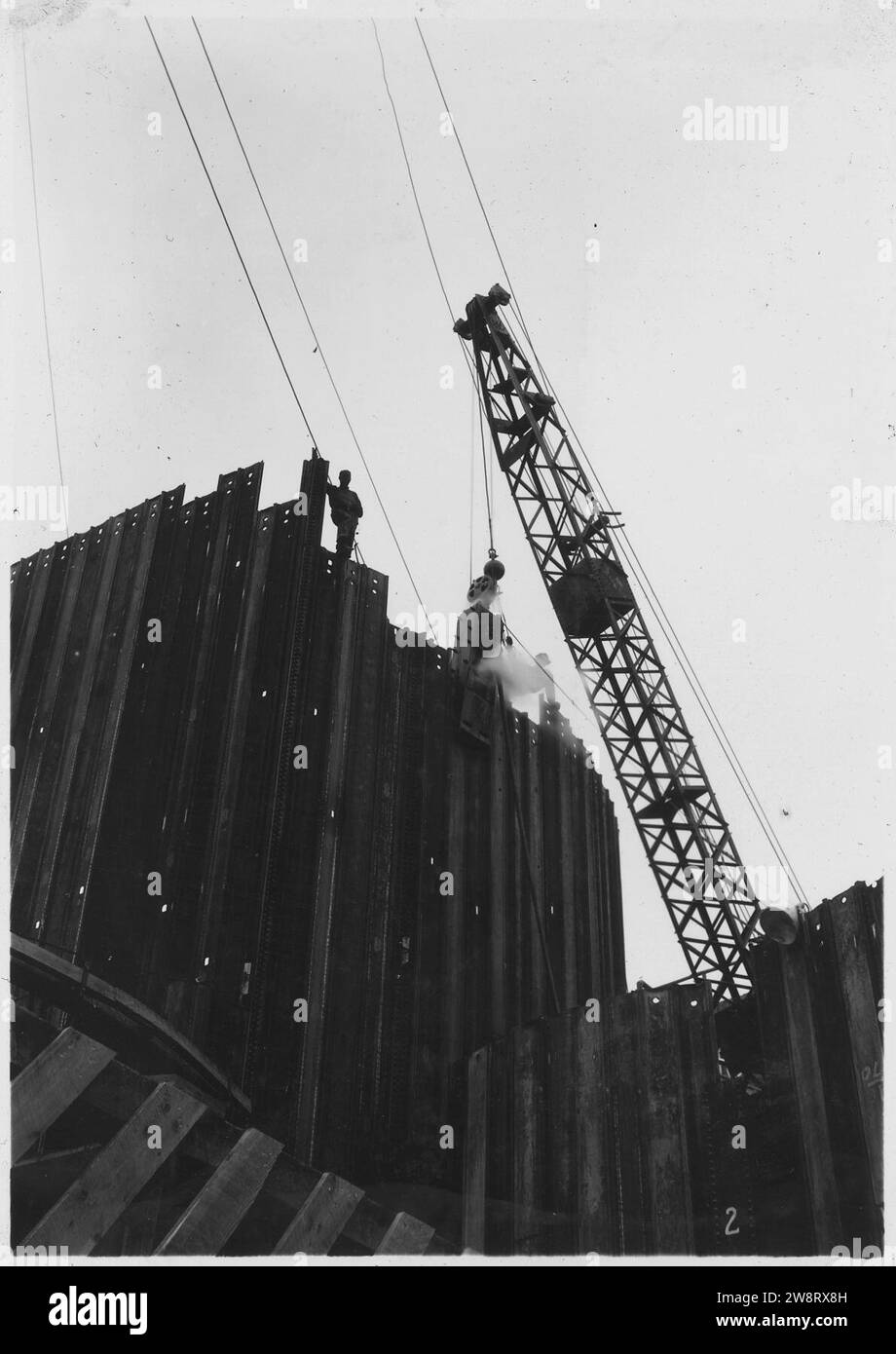 Workman in bosun's chair placing sheet piling in caissons of cofferdam ...