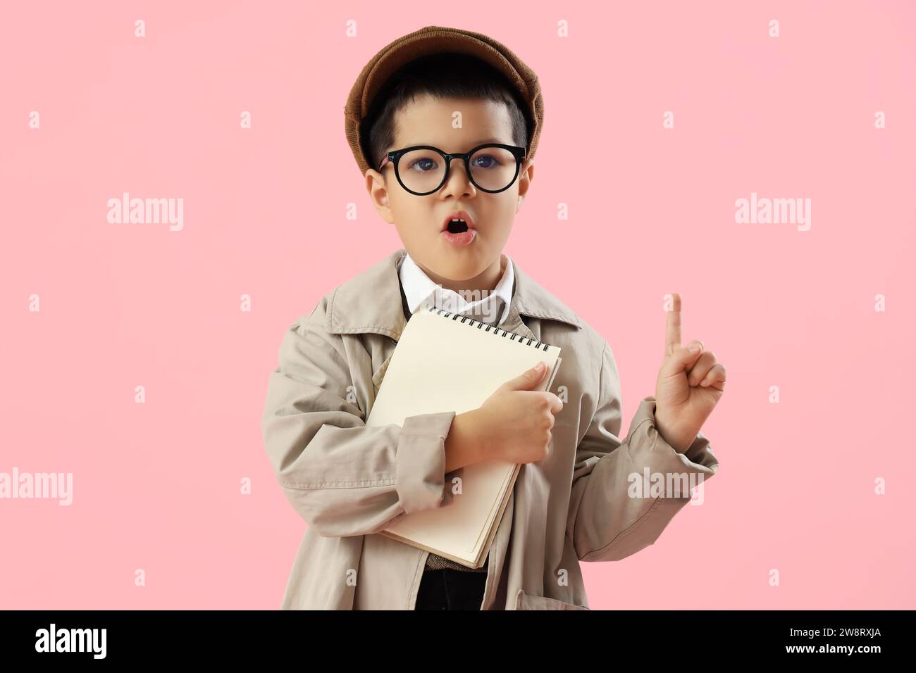 Shocked little detective with notebook pointing at something on pink ...