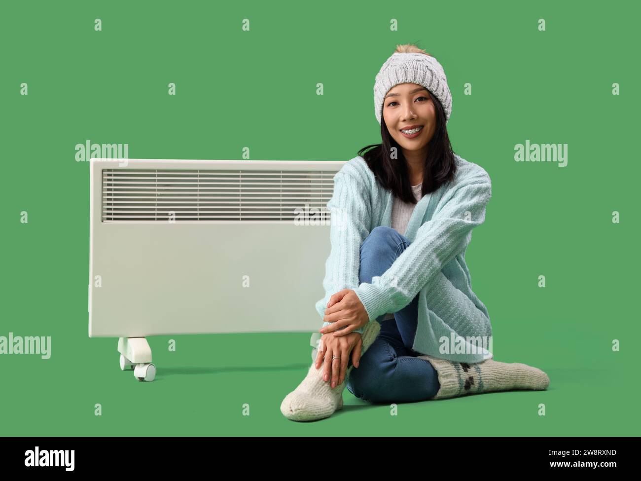 Young Asian woman in winter clothes with radiator sitting on green ...
