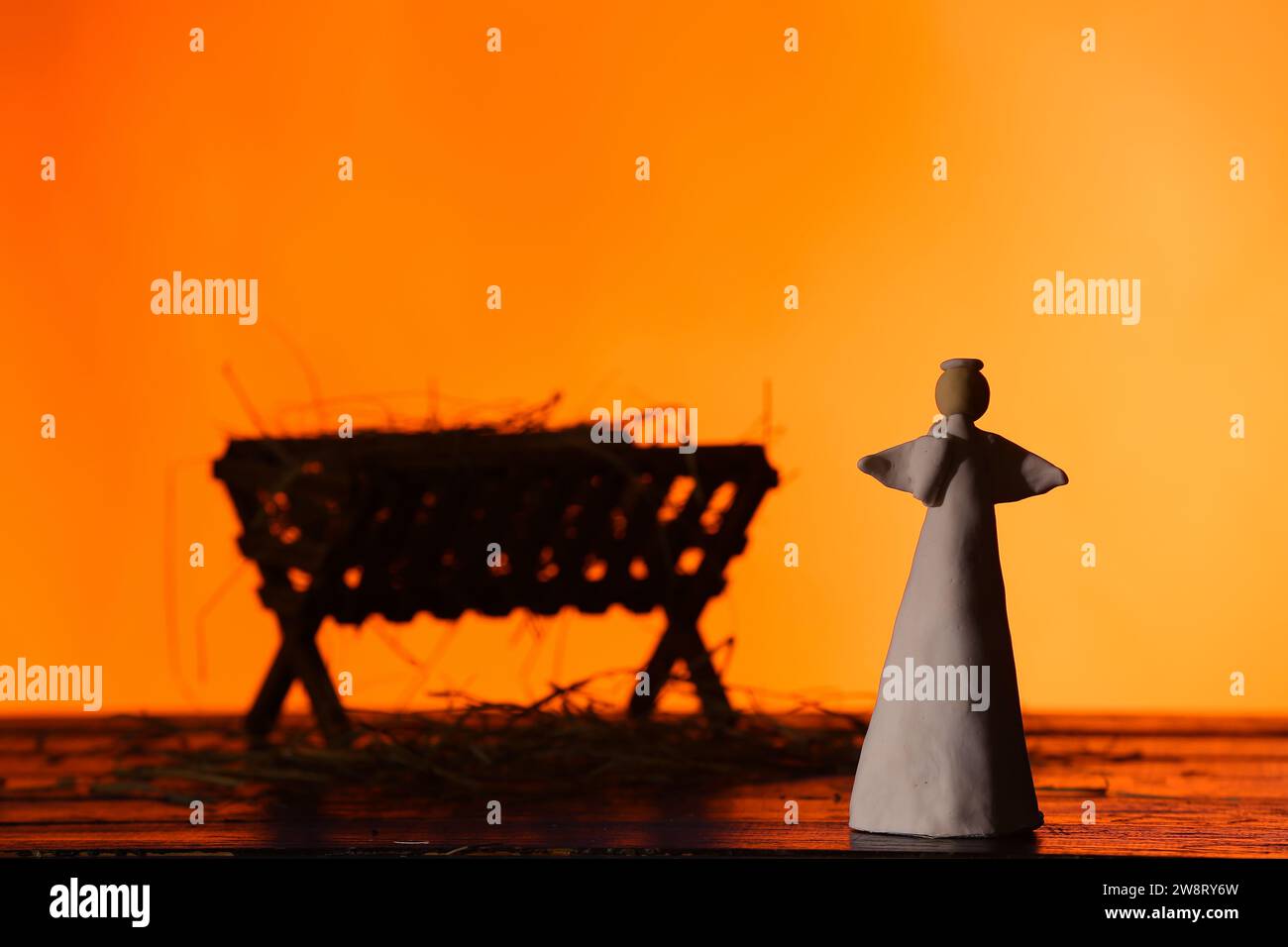Manger with hay and angel on table against orange background. Concept ...