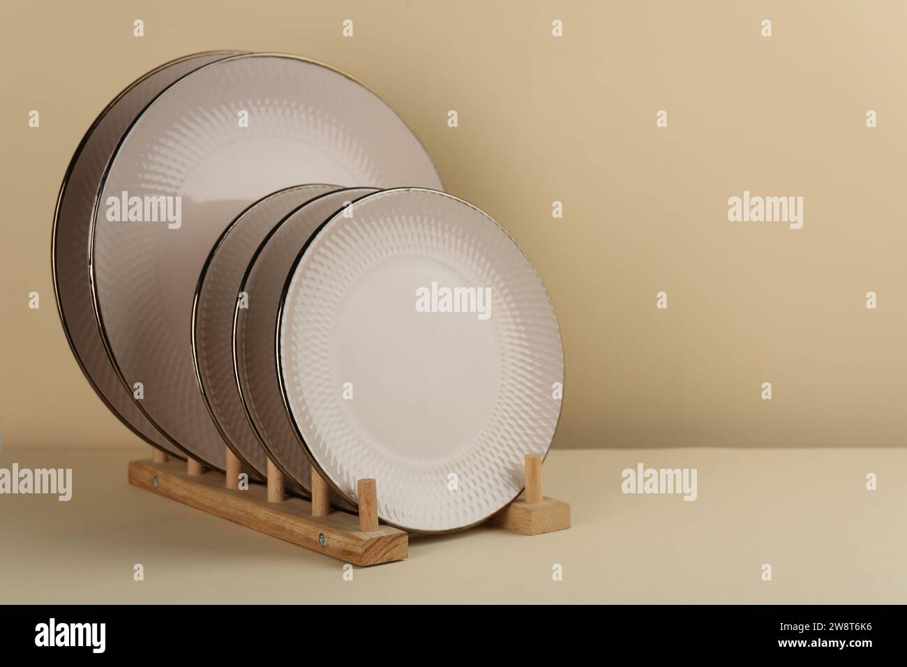Drying rack with beige ceramic plates on pale yellow table, space for ...