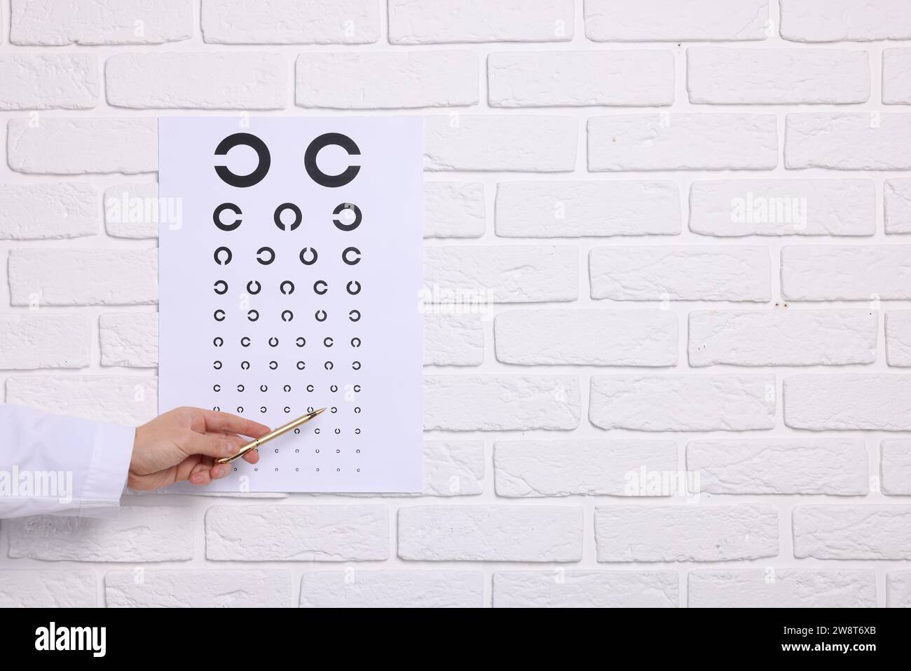 Ophthalmologist pointing at vision test chart on white brick wall ...