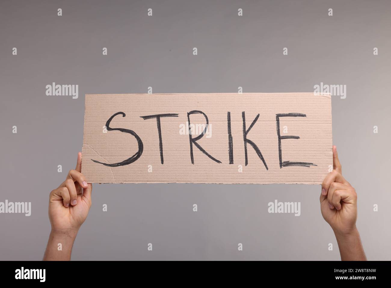 Man holding cardboard banner with word Strike on grey background ...