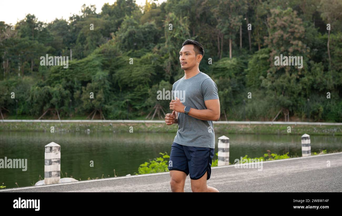 A handsome, focused Asian man in sportswear is running outdoors in the ...