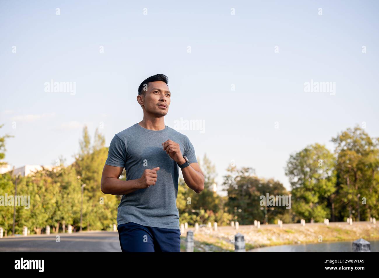 A fit and strong Asian man in sportswear is running on the street in a ...
